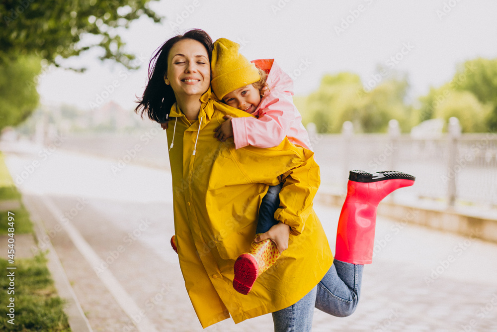 Mother with daughter walking in park in the rain wearing rubber boots ...