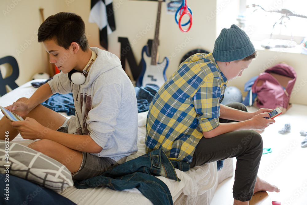 Two teenage boys using electronic devices in room Stock Photo | Adobe Stock