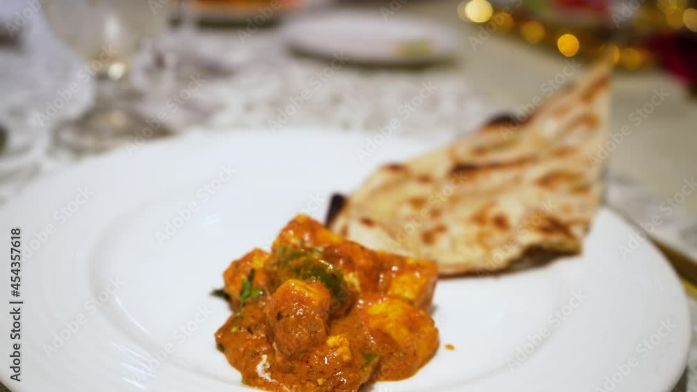 overhead panning shot of a white plate with paneer cottage cheese gravy ...