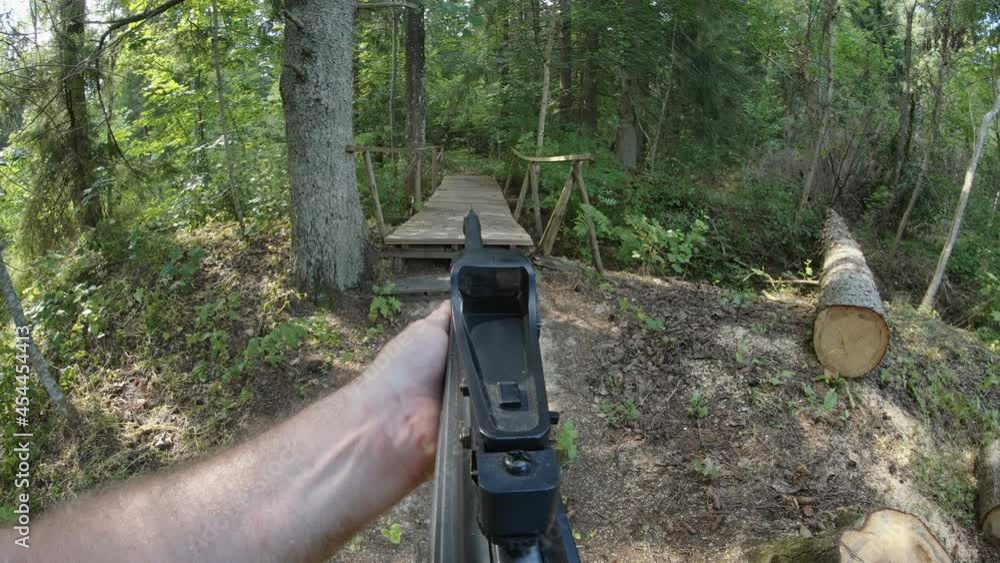 The man holding the black rifle gun pointing on the trees in the forest ...