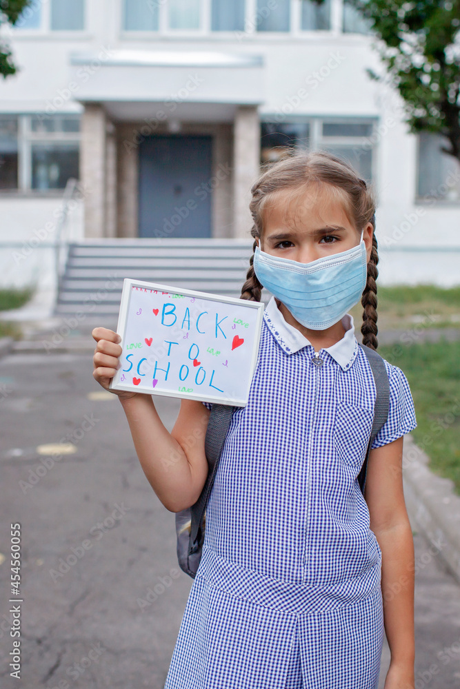 Elementary school girl in medical mask holds picture with back to ...