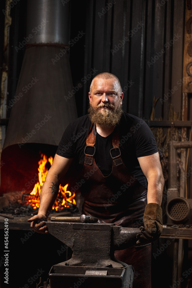 Bearded man, blacksmith manually forging the molten metal on the anvil ...