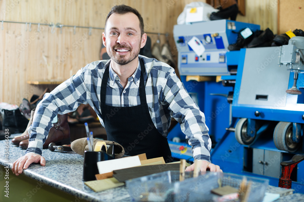 Happy man worker displaying his workplace and tools in shoe repair ...