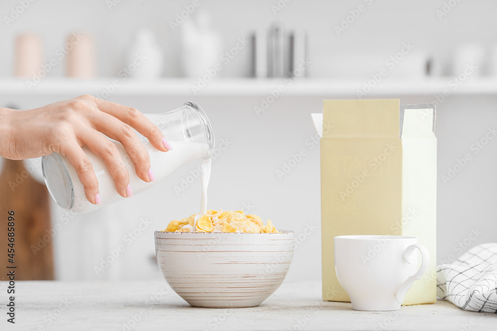 Woman pouring milk from bottle into bowl with corn flakes on table in ...