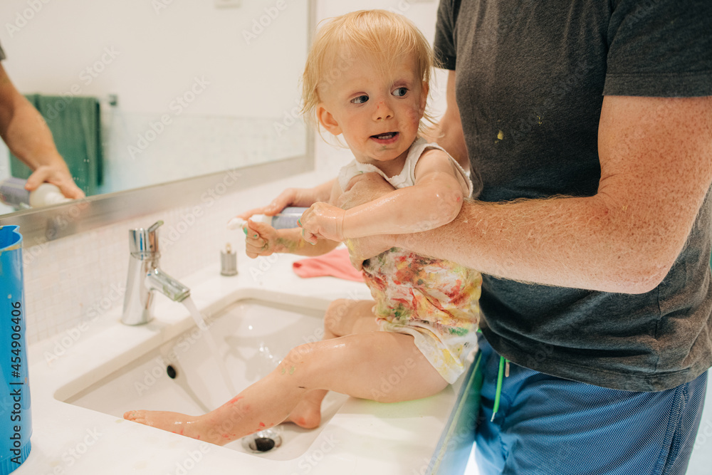 Father washing little girl in bathroom sink. Portrait of messy baby ...