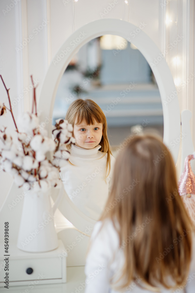 Little girl child looking in the mirror at home in a white dress. Stock ...