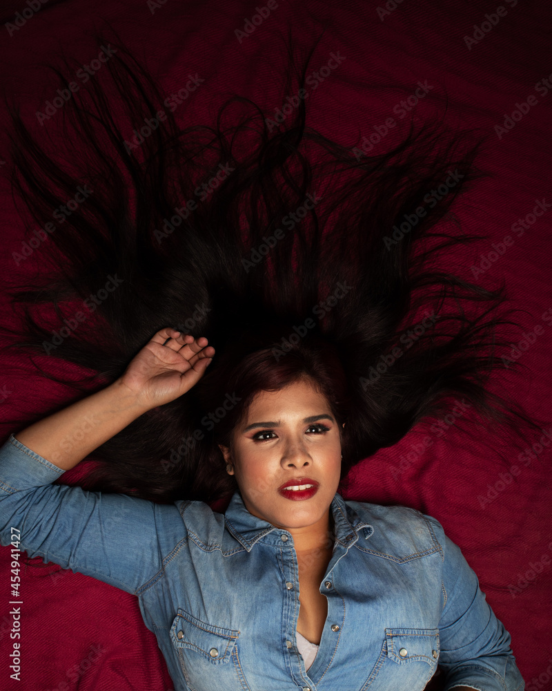 Chica acostada mirando hacia arriba con cabello suelto en fondo rojo ...