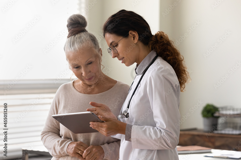 Serious GP doctor showing tablet screen to old 70s female patient ...