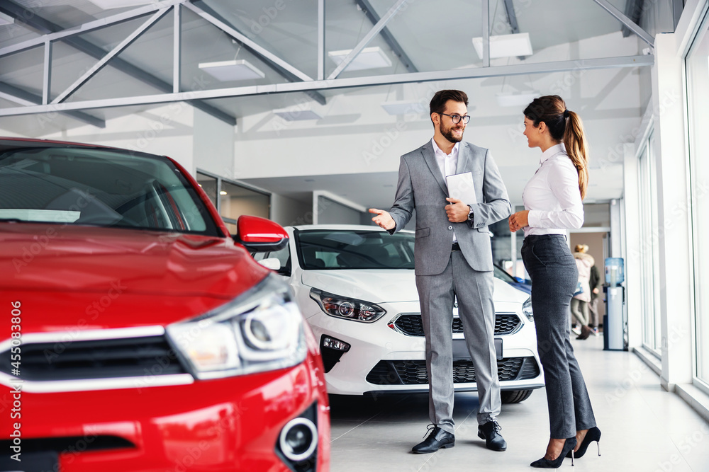 Smiling car seller standing in car salon with customer and showing ...