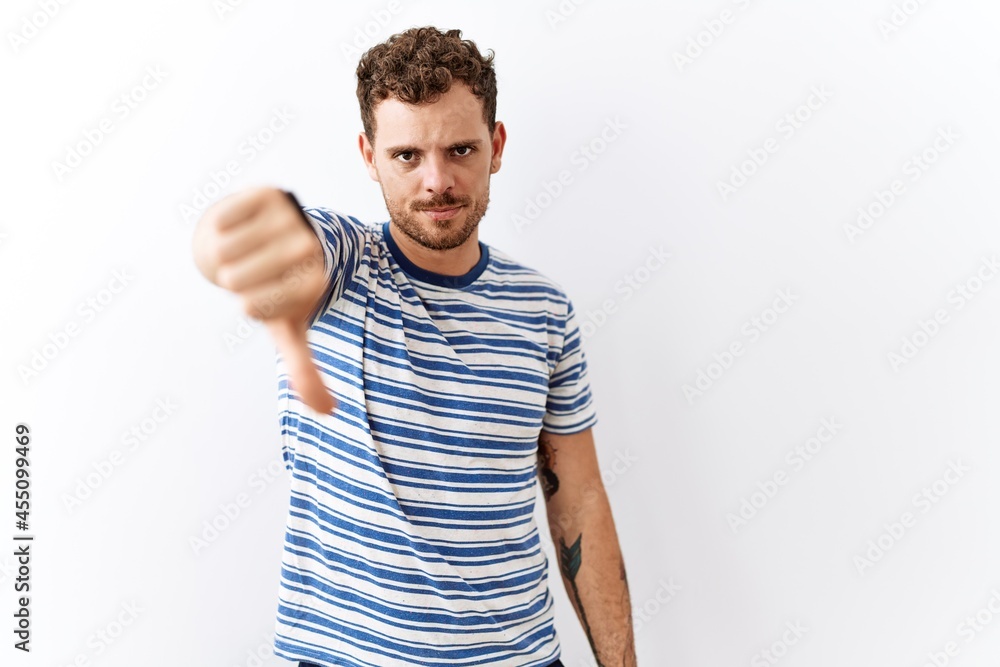 Handsome young man standing over isolated background looking unhappy ...