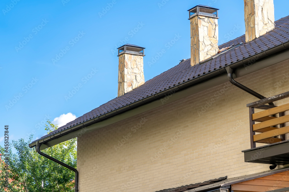 Brick house with drainage system on metal roof. Сhimney pipes is ...