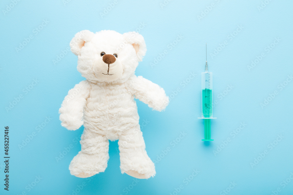White teddy bear and syringe on light blue table background. Pastel ...