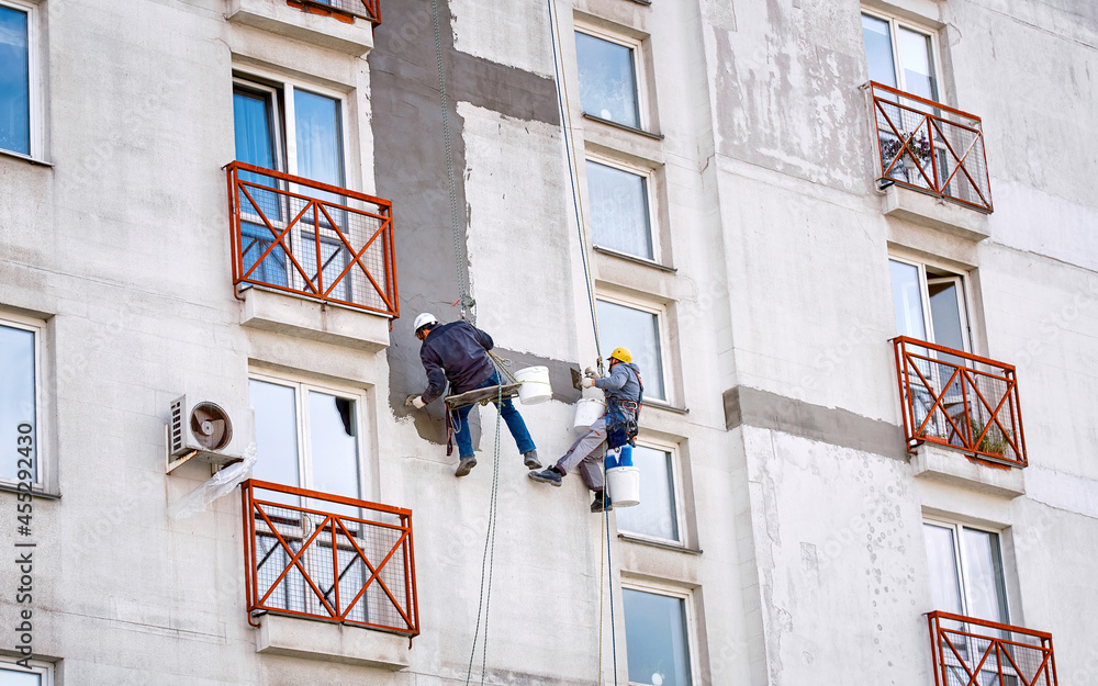 Industrial alpinists at height on rope, plastering wall with trowel ...