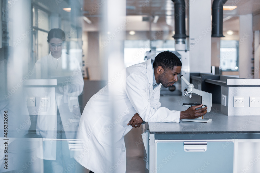 African American male scientist looking through microscope in a ...