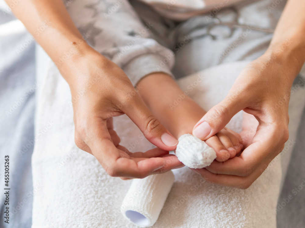 Mother bandages her child's big toe. Close-up photo of kid's foot with ...