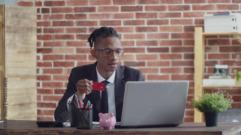 Black man in glasses and a suit enters the bank card data into a laptop ...