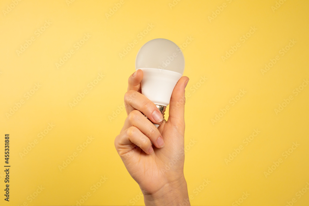 Mano sosteniendo foco, fondo amarillo. Stock Photo | Adobe Stock