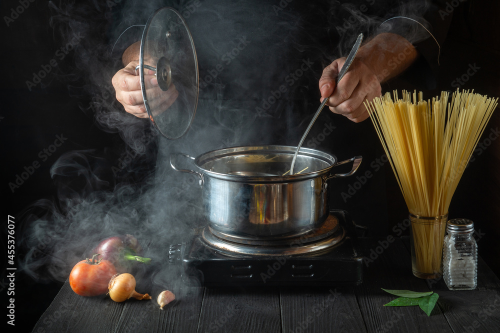Cook prepares Italian pasta in a saucepan with vegetables. Close-up of ...