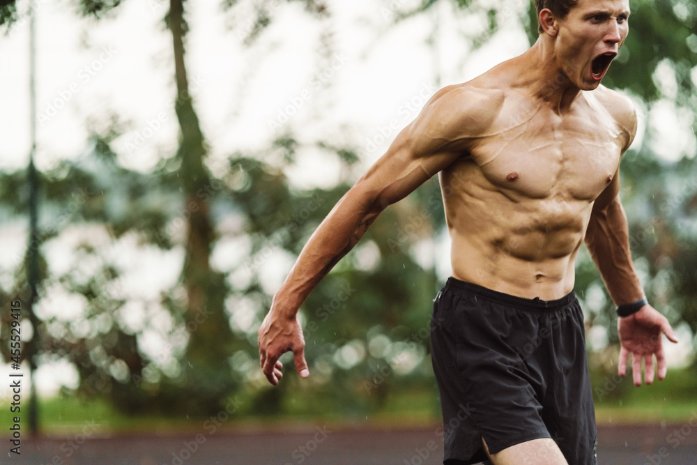 Young shirtless sportsman screaming while working out on playground ...