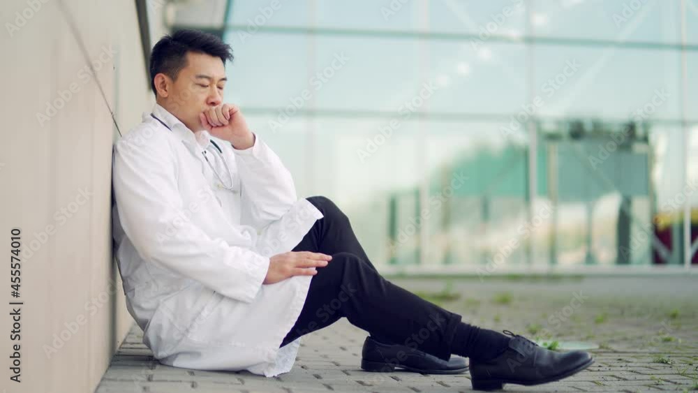 portrait stressful Asian doctor sitting or standing outside a hospital ...
