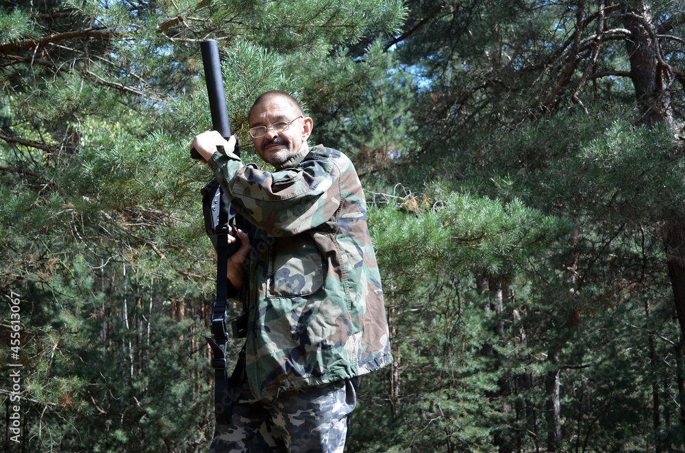 Mature man with 9mm caliber submachine gun with silencer in the forest ...