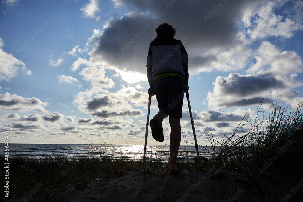 Silhouette of a little boy standing with crutches on the beach. Stock ...