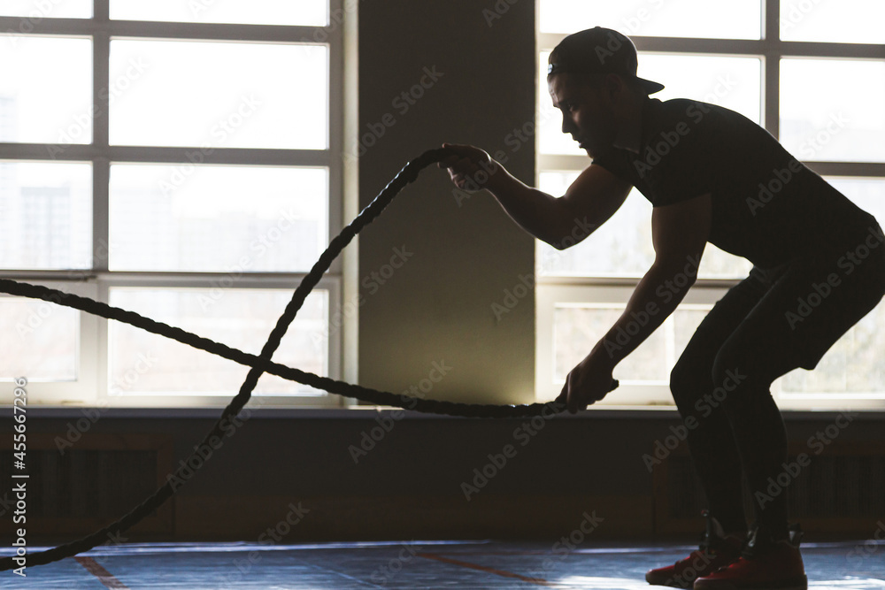 Crossfit with ropes. The athlete is training in the gym. Silhouette ...