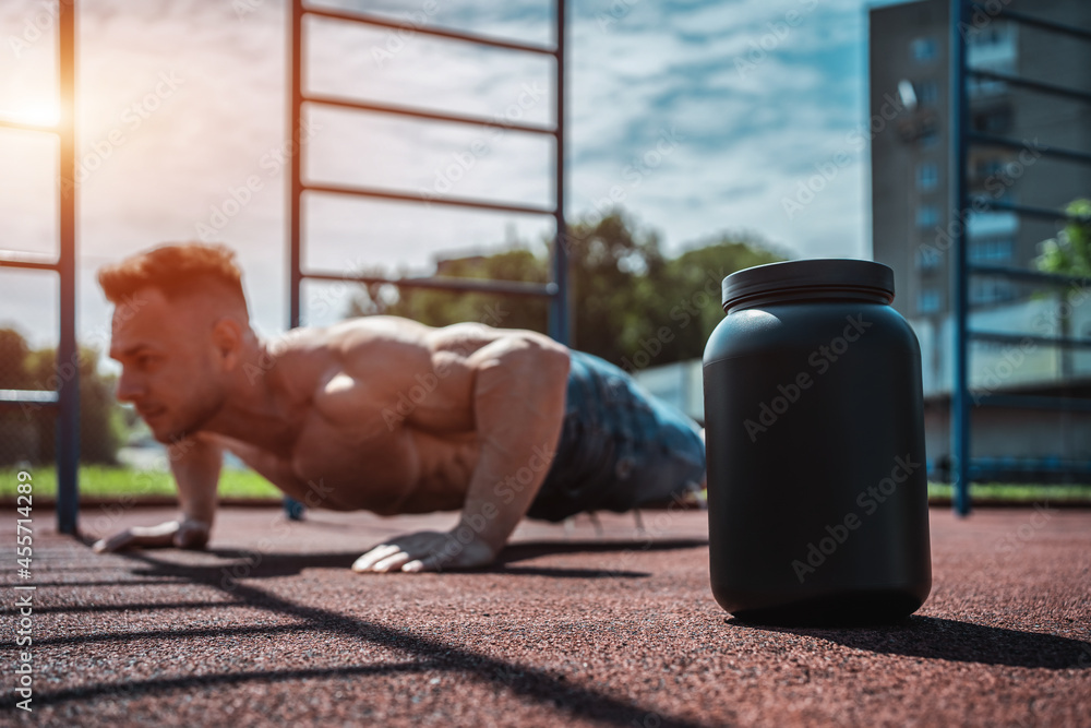 protein whey drink in black container and muscular athlete exercising ...
