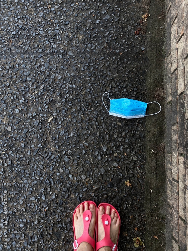 Person wearing red flip flops standing next to blue face mask on ...