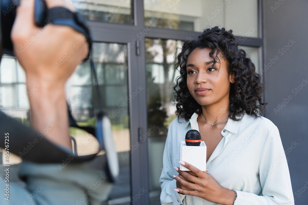 curly african american journalist with microphone gesturing while doing ...