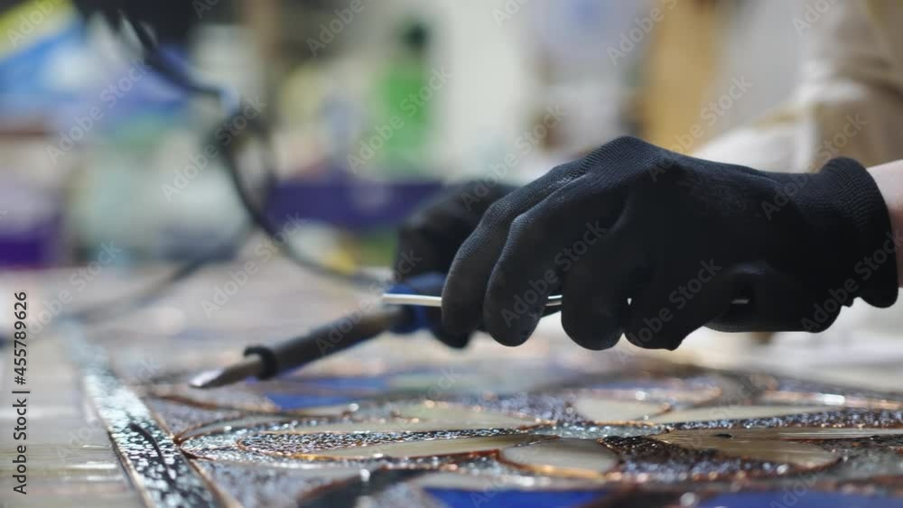 Close-up Soldering stained glass seams. Gloved artist's hands with a ...
