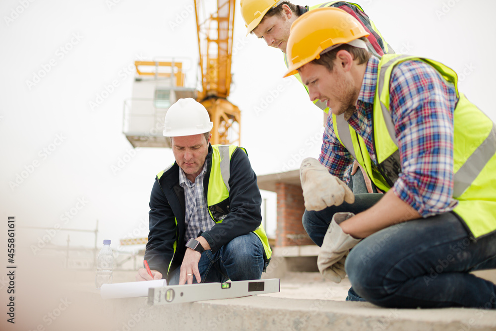 Construction workers using level tool below crane at construction site ...