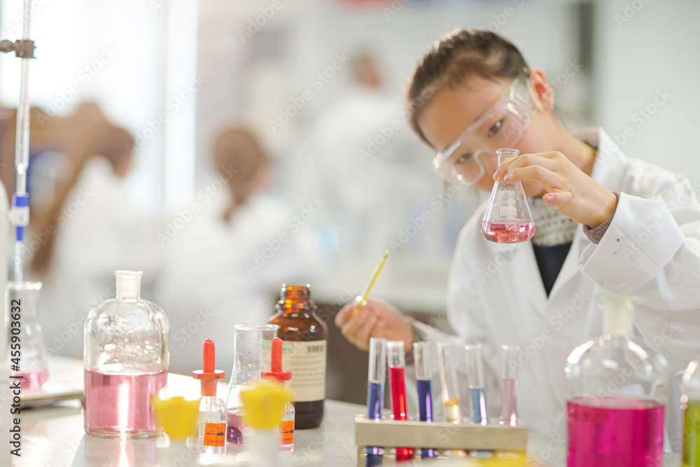 Girl student examining pink liquid, conducting scientific experiment in ...