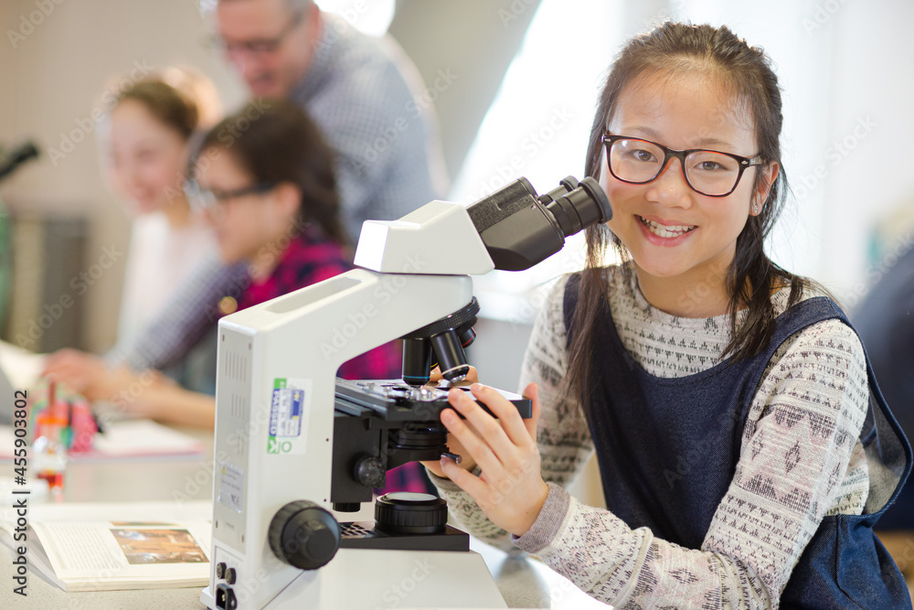 Portrait smiling, confident girl student using microscope, conducting ...