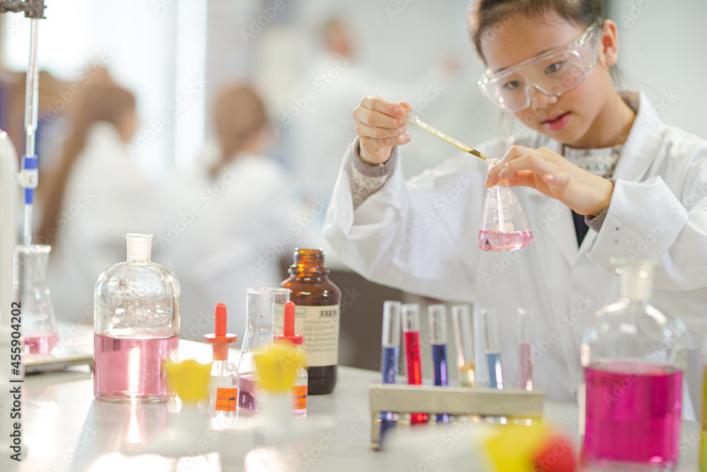 Girl student examining pink liquid, conducting scientific experiment in ...
