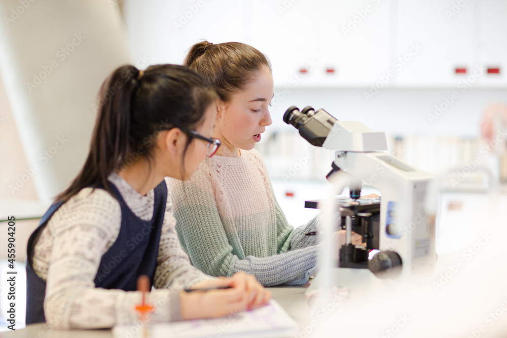 Girl student conducting scientific experiment at microscope in ...