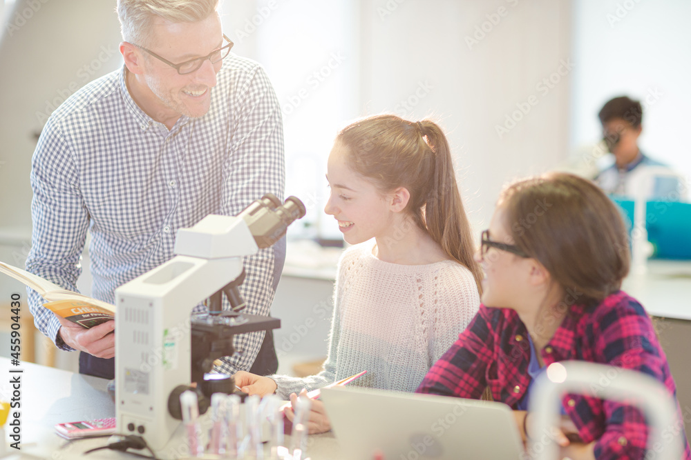 Male teacher helping girl students using microscope, conducting ...