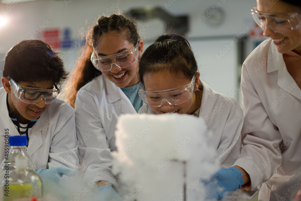 Female teacher and students watching scientific experiment chemical ...