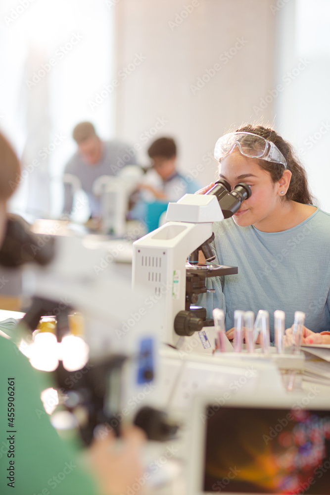 Girl student conducting scientific experiment at microscope in ...