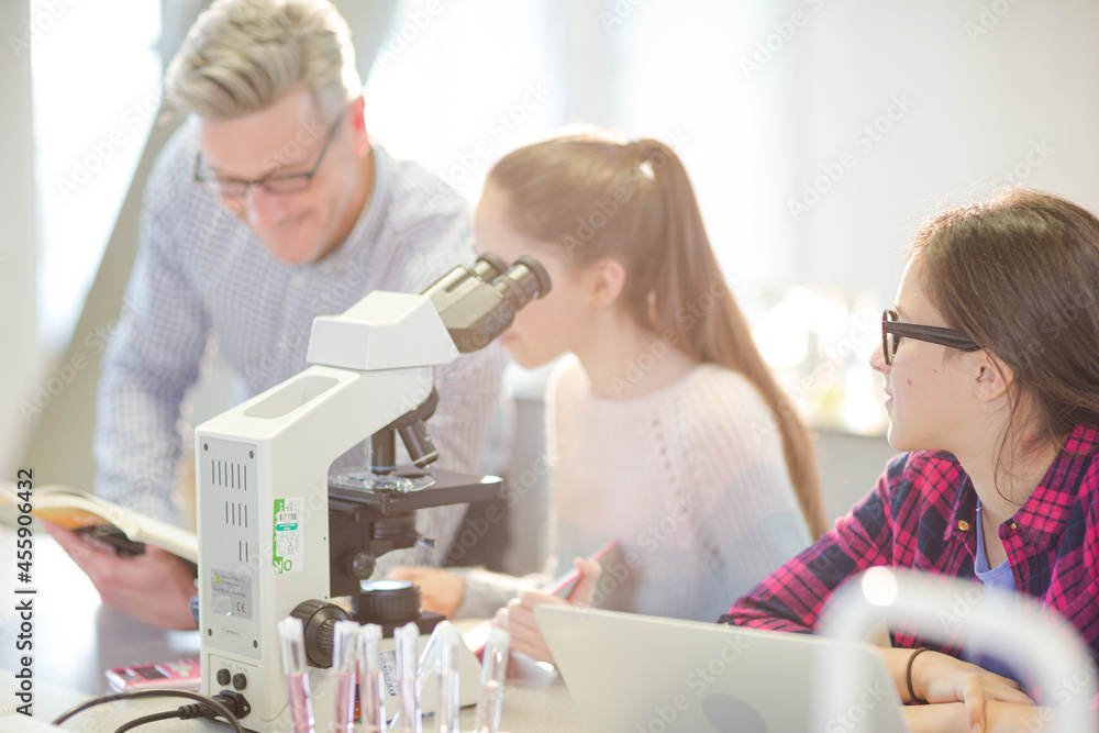 Male teacher helping girl students using microscope, conducting ...