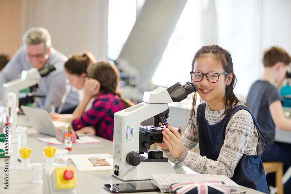 Portrait smiling, confident girl student using microscope, conducting ...