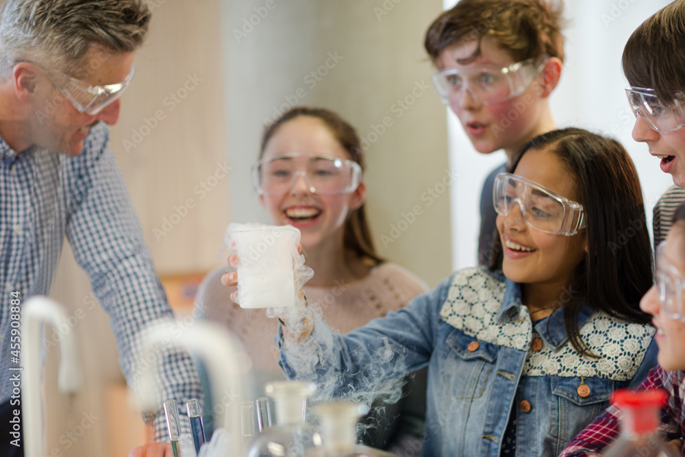 Male teacher and students watching chemical reaction, conducting ...