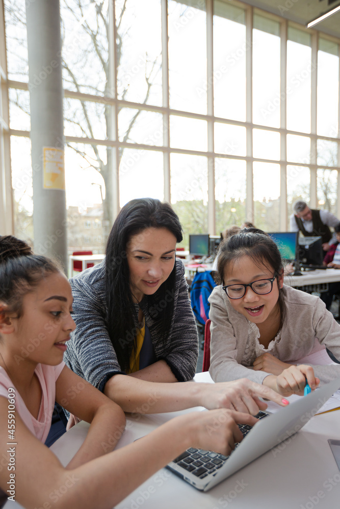 Female teacher and girl students using laptop at table Stock Photo ...