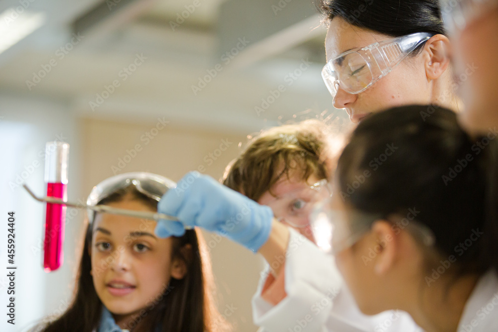Female teacher and students examining liquid in test tube, conducting ...