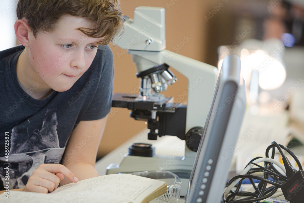 Boy student conducting scientific experiment at microscope and computer ...