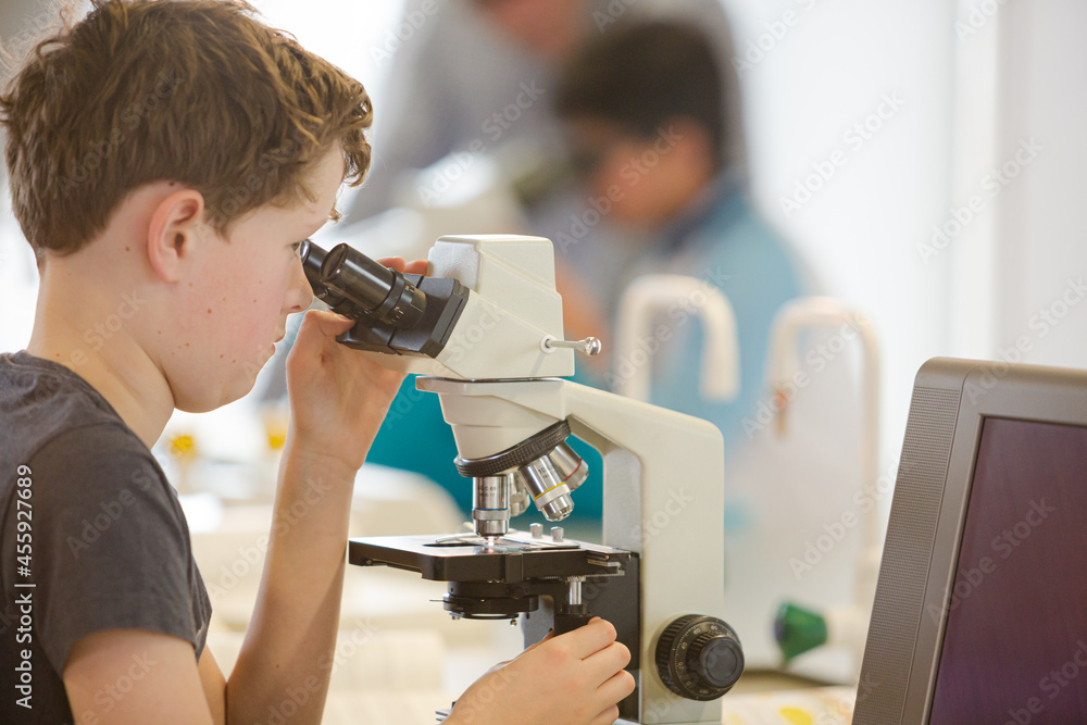 Boy student conducting scientific experiment at microscope and computer ...