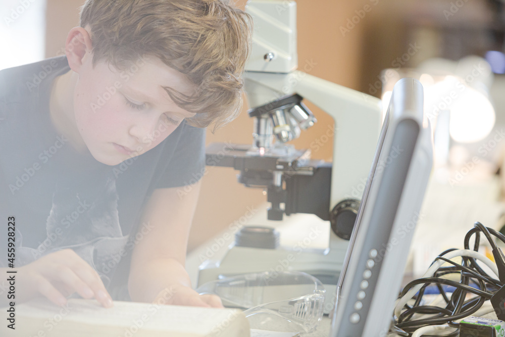 Boy student conducting scientific experiment at microscope and computer ...