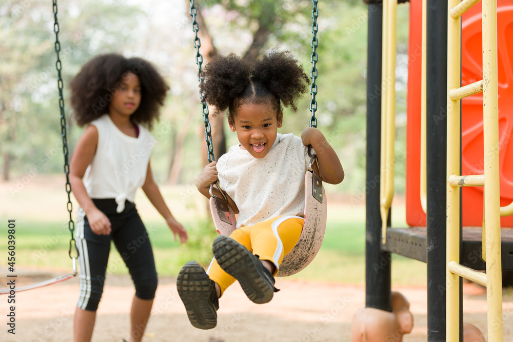 Happy cheerful African American child girl playing on swing at ...