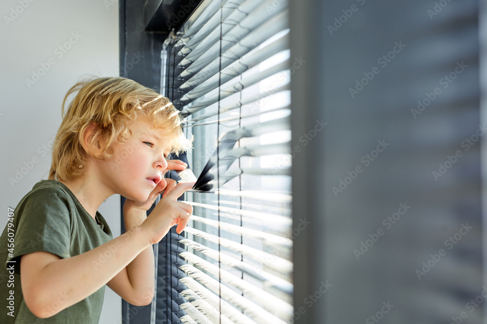offended little caucasian boy looks out the window, lowers the blinds ...