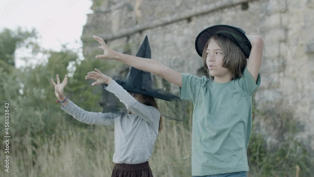 Stockvideon Side view of boy and girl conjuring in witch hats in nature ...